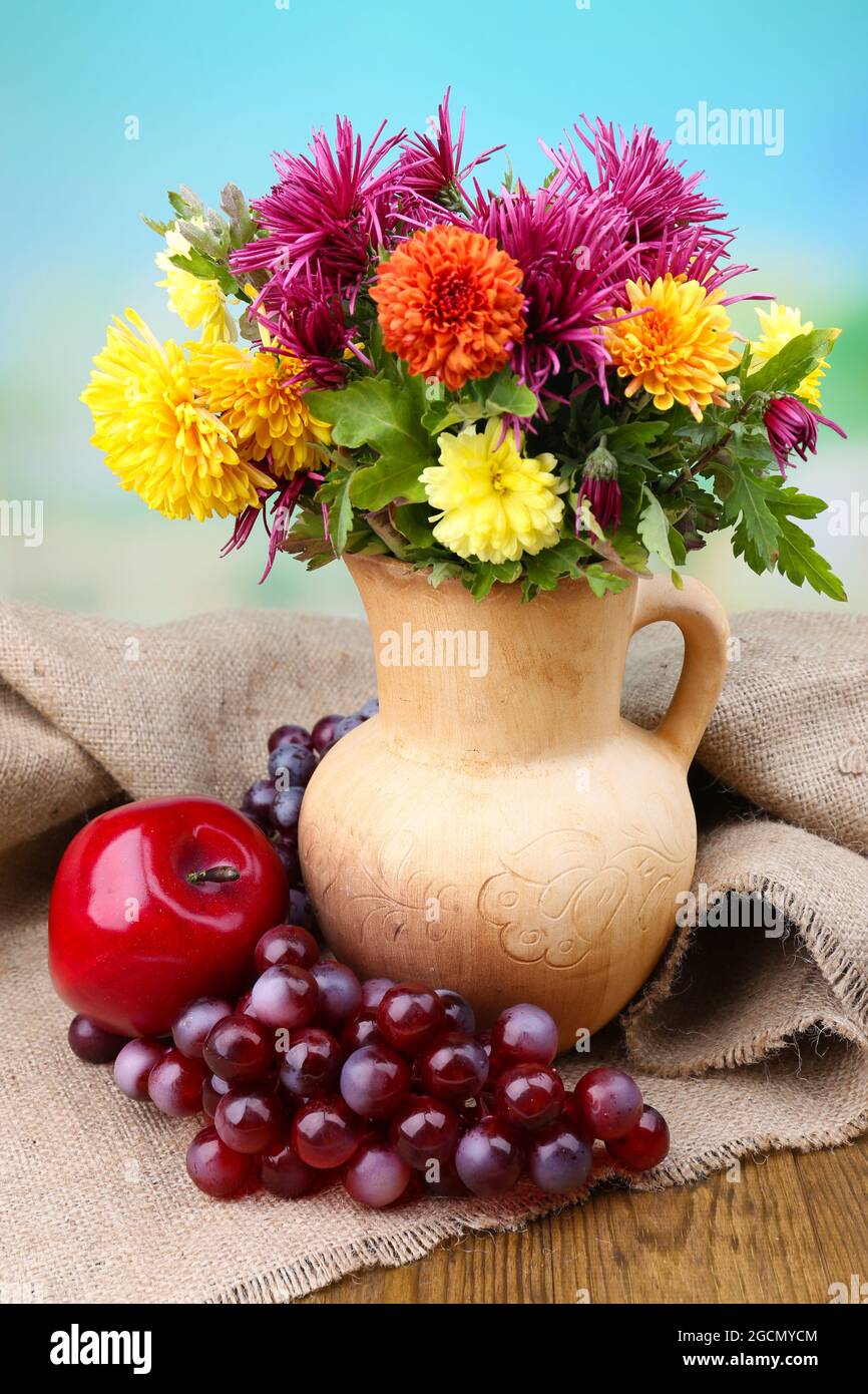 Composition with beautiful flowers in pitcher, and fruits, on bright ...