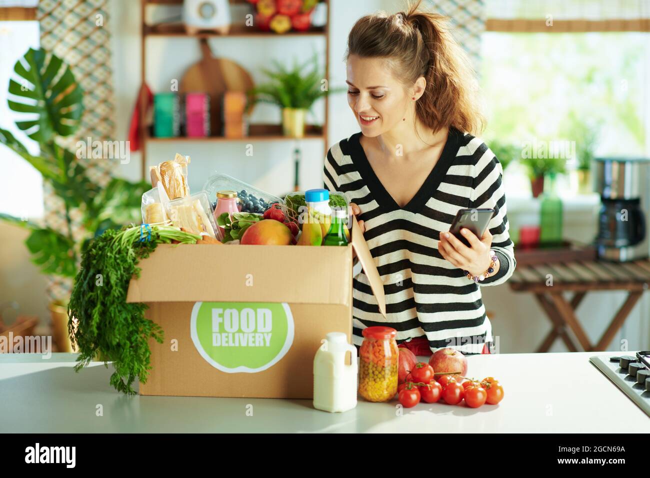 Food delivery. happy young woman with food box using smartphone ...