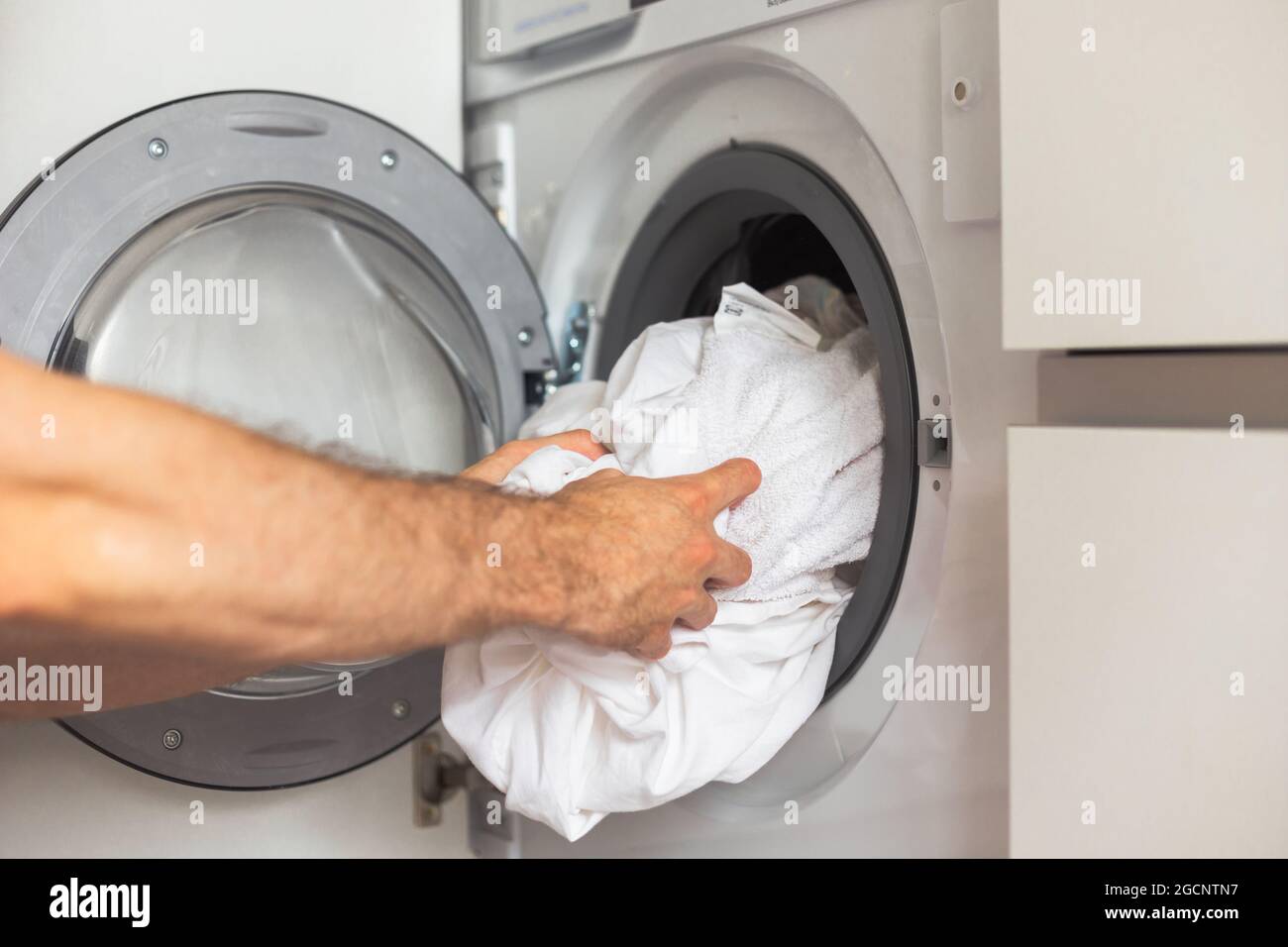 Housework: Man loading white clothes into washing machine Stock Photo ...