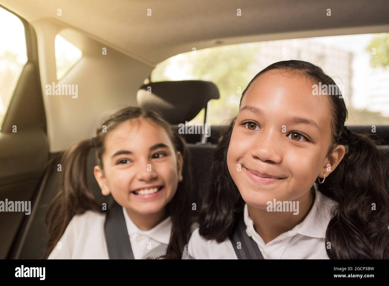 Two smiling little Hispanic schoolgirls in the backseat of the car ...