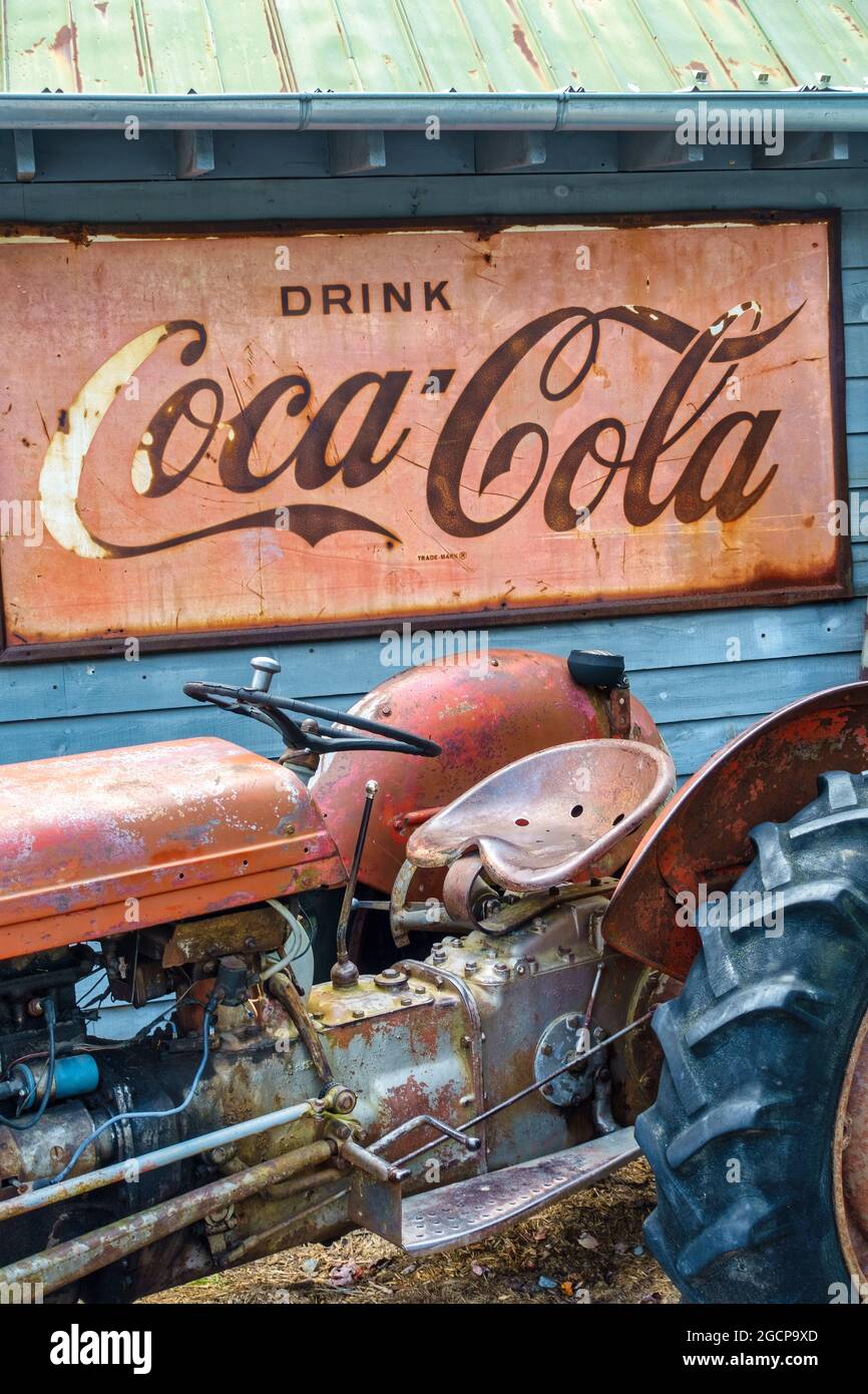 A vinatge tractor parked under a rusted sign for Coca Cola at the Mast ...