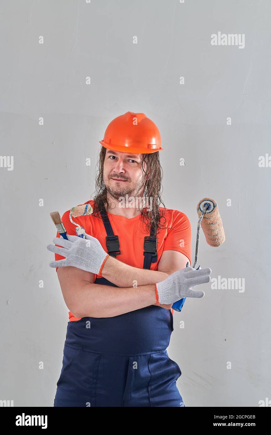 a builder stands in overalls with a roller and a brush Stock Photo - Alamy
