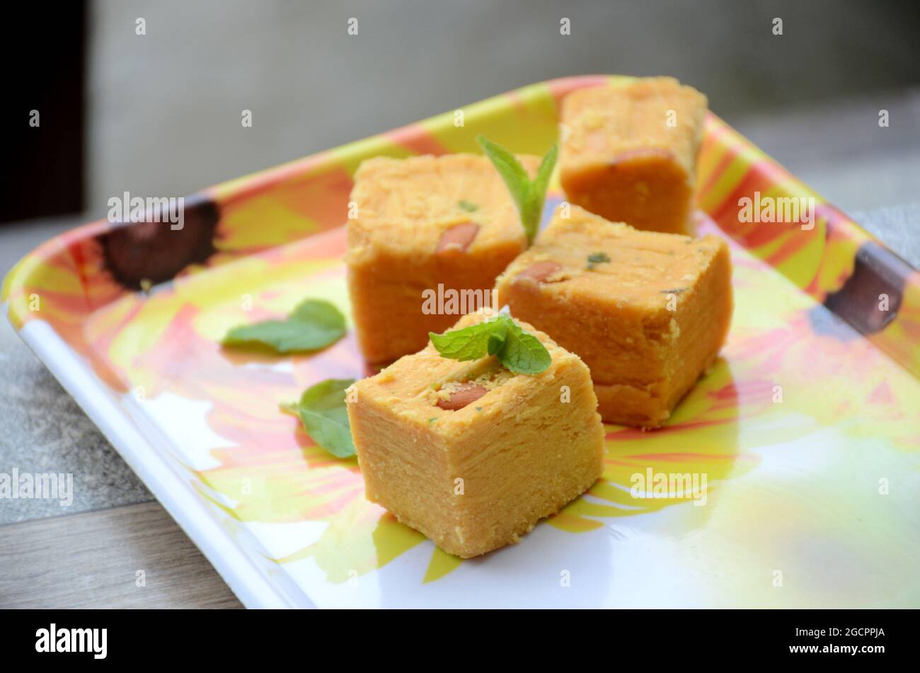 closeup the yellow gram flour sweet with green mint over out of focus ...