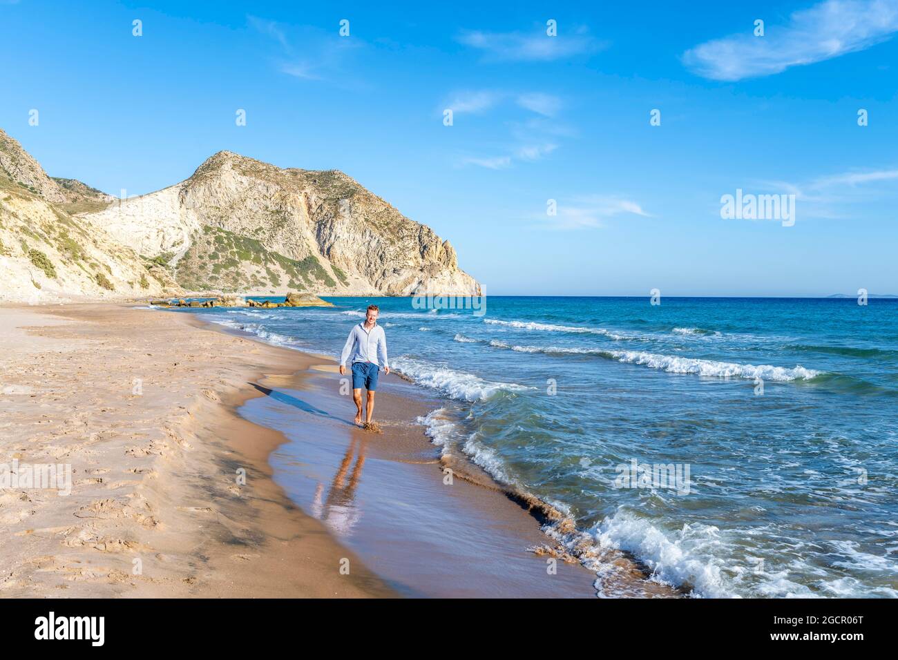 Young man walking on a beach, sandy beach with rocky cliffs, Paralia ...