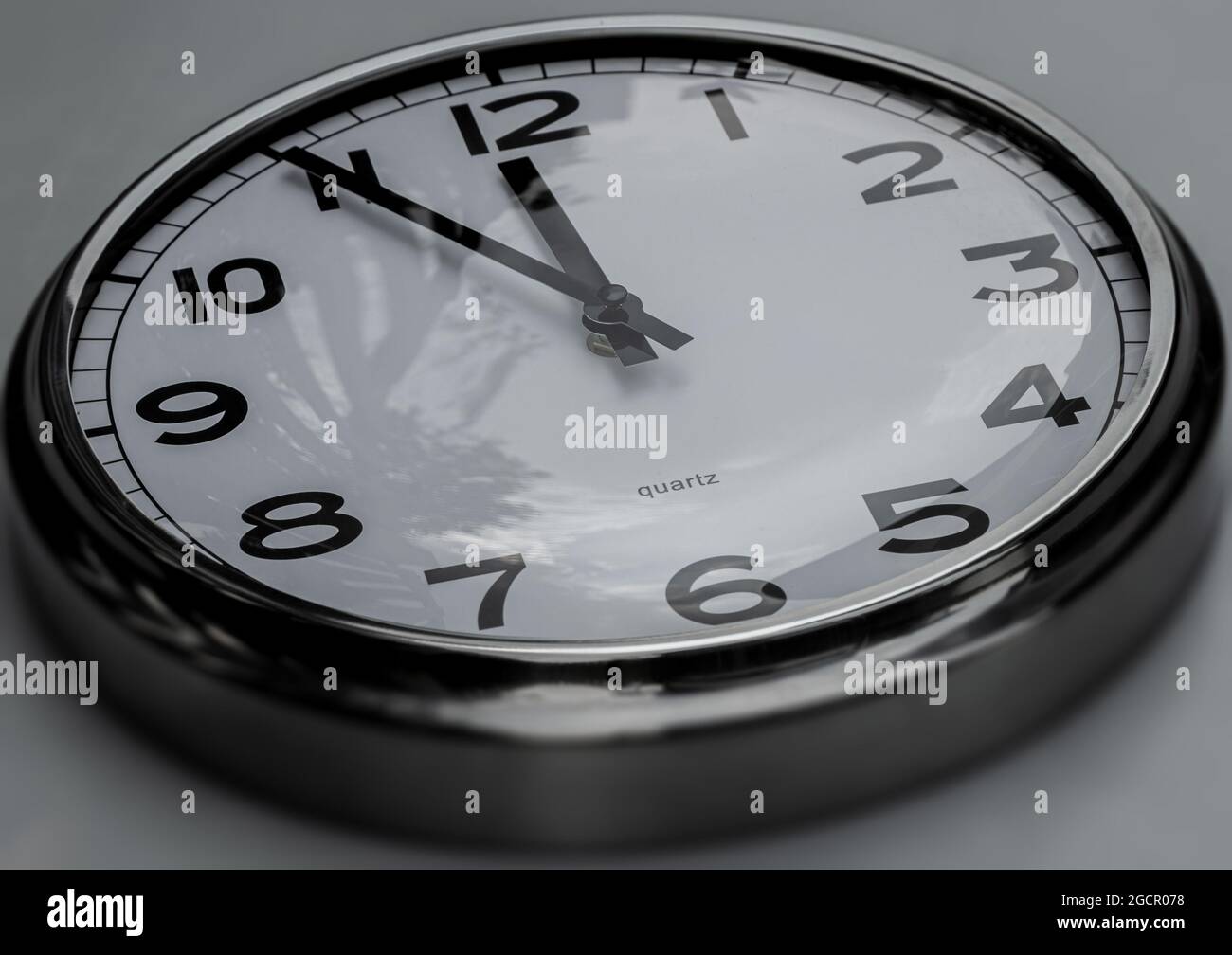 A Modern white aluminum wall clock in sunlight with shadows on the ...