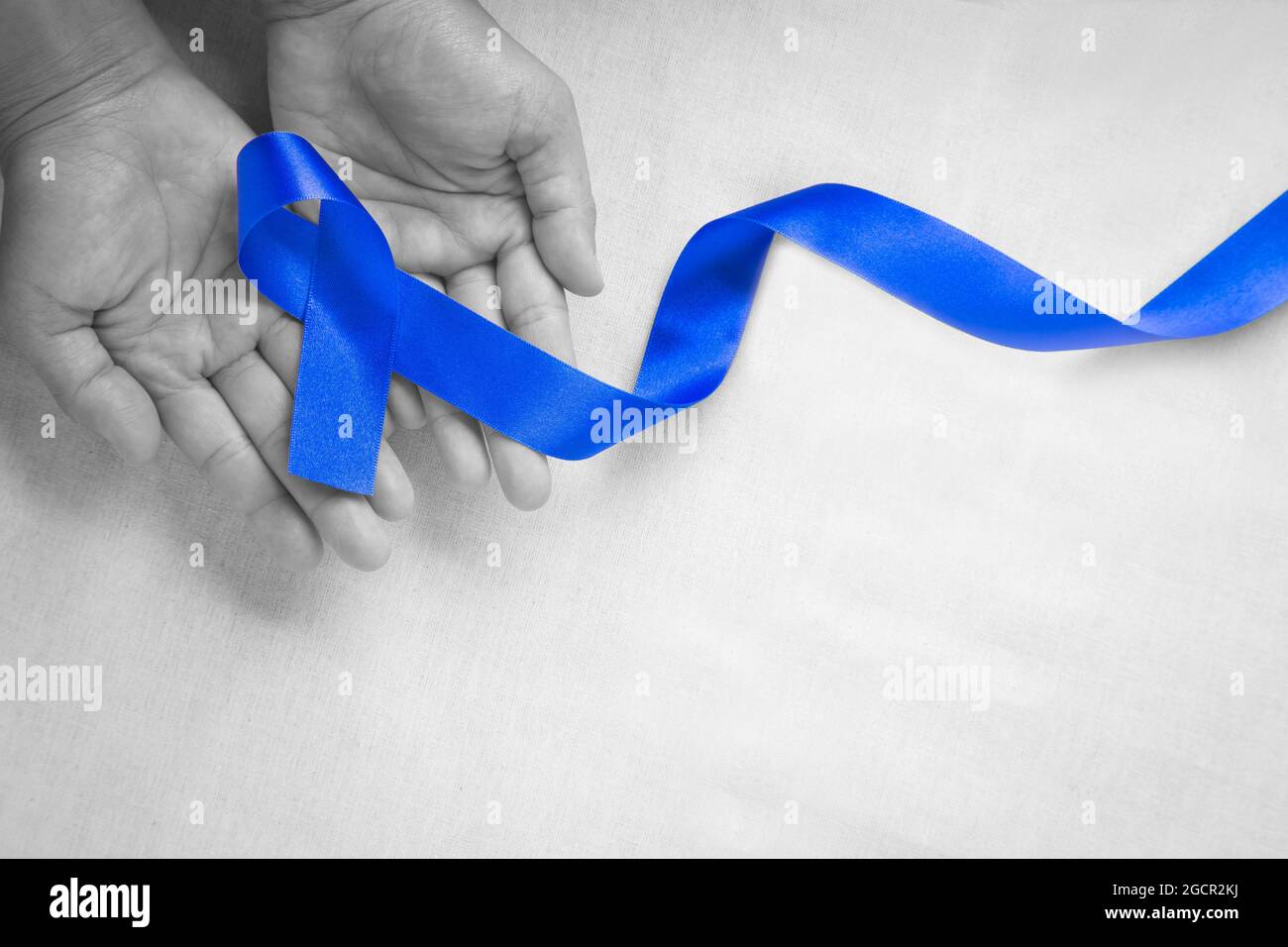 Hands Holding Deep Blue Ribbon On White Fabric With Copy Space