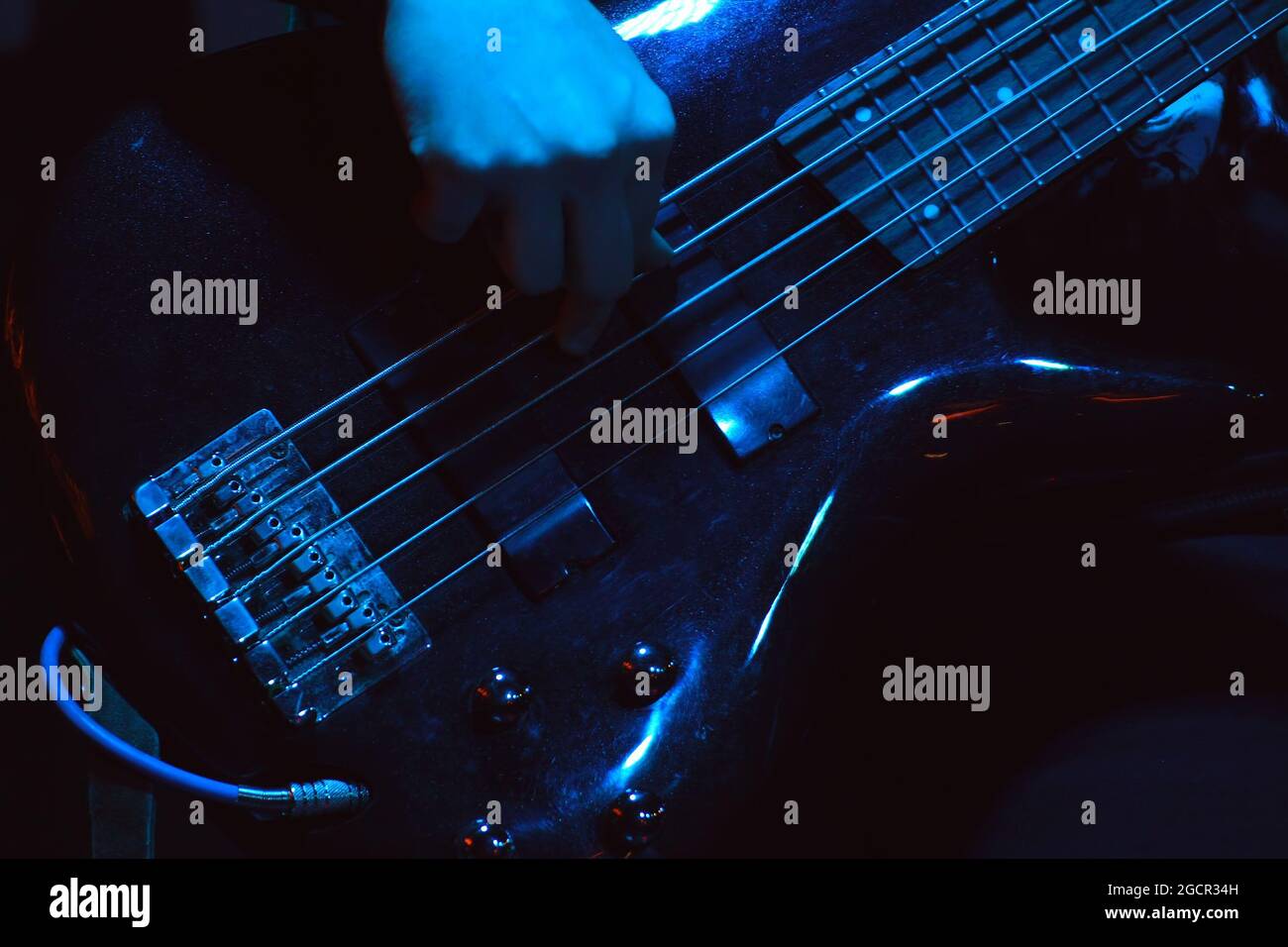 The bass player plays on black five-string bass guitar in the spotlight ...