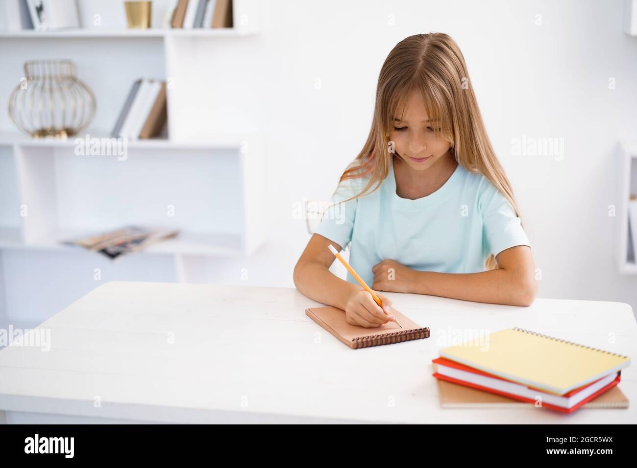 Teenage girl making notes in notepad, doing homework at table at home ...