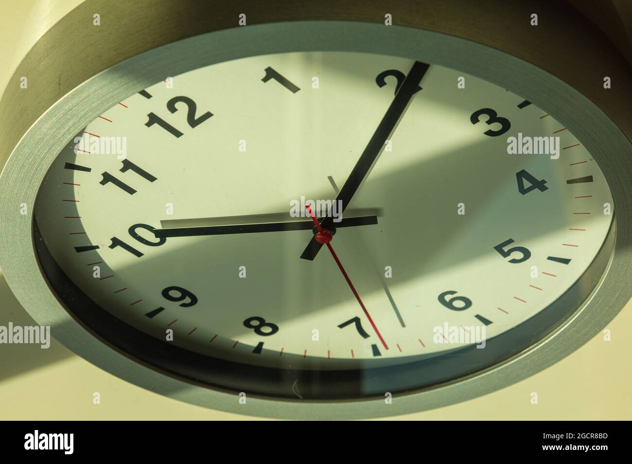 A Modern white wall clock in sunlight with shadows on the clock face ...