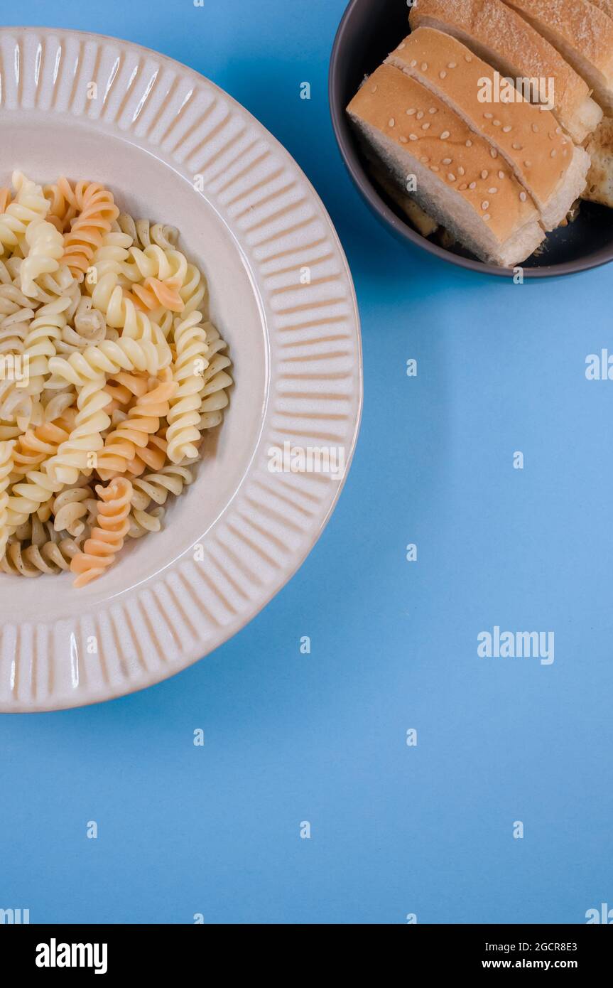 Plate of pasta twists and a bowl of sliced bread on a blue background ...
