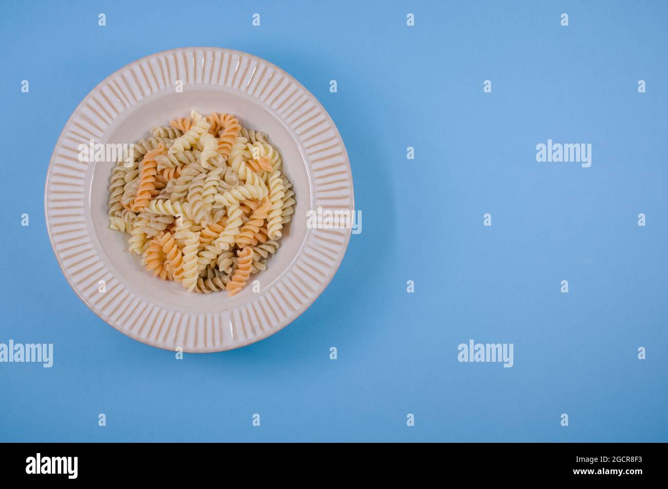 Plate with pasta twists isolated on a blue background with free space ...