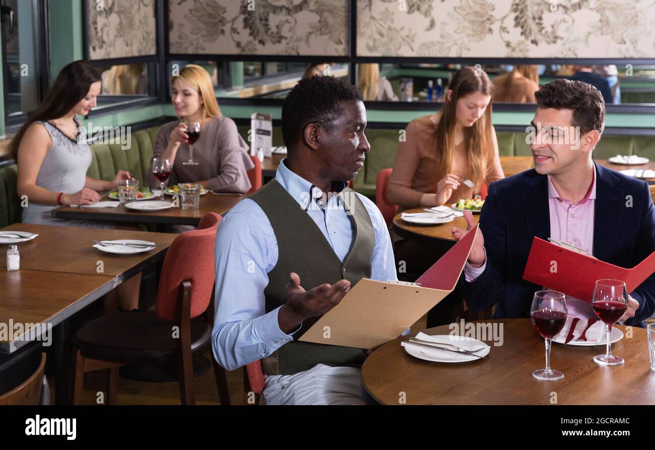 Cheerful male friends choosing dishes from menu card in restaurant ...