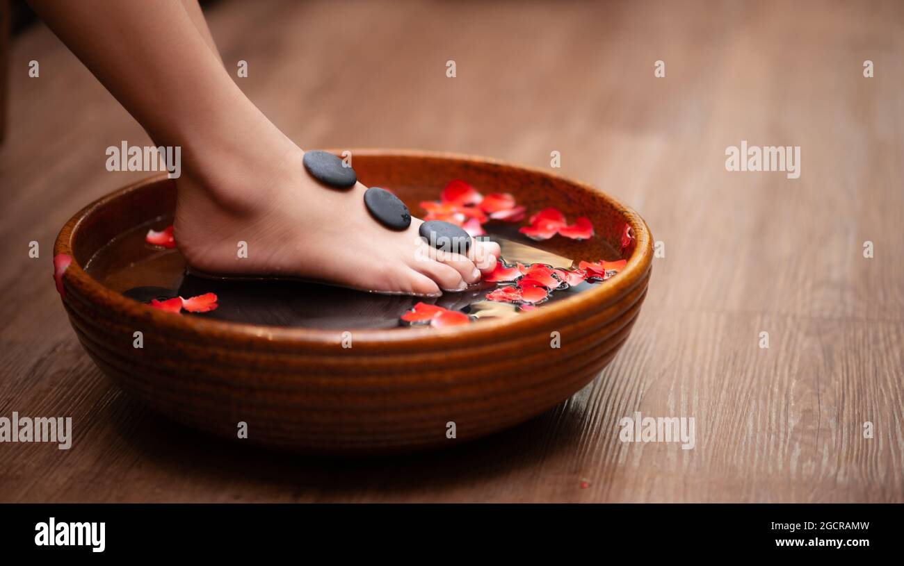 woman feet dipped in water with petals in a wooden bowl. Beautiful ...