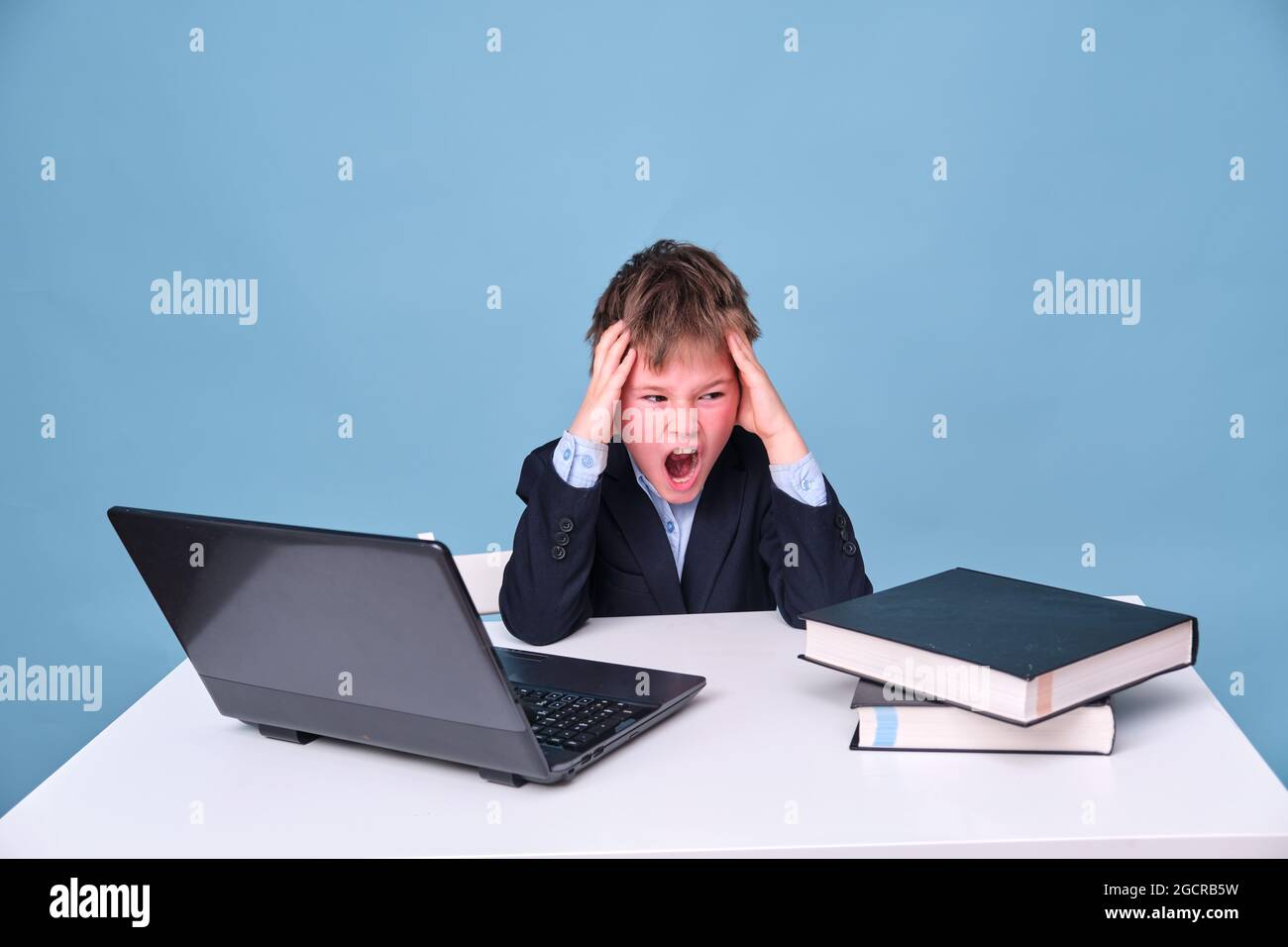 Angry boy in a school suit on distance learning, copy space on a blue ...