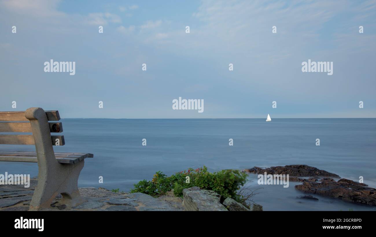 Lone empty bench, facing distant sailboat on smooth ocean Stock Photo ...