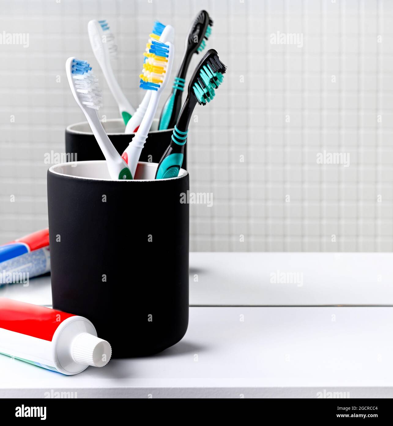 Toothbrushes in a black glass and toothpaste in front of a mirror on ...