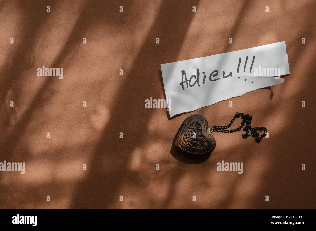 Handwritten word Adieu in a white piece of paper and a wooden amulet in ...