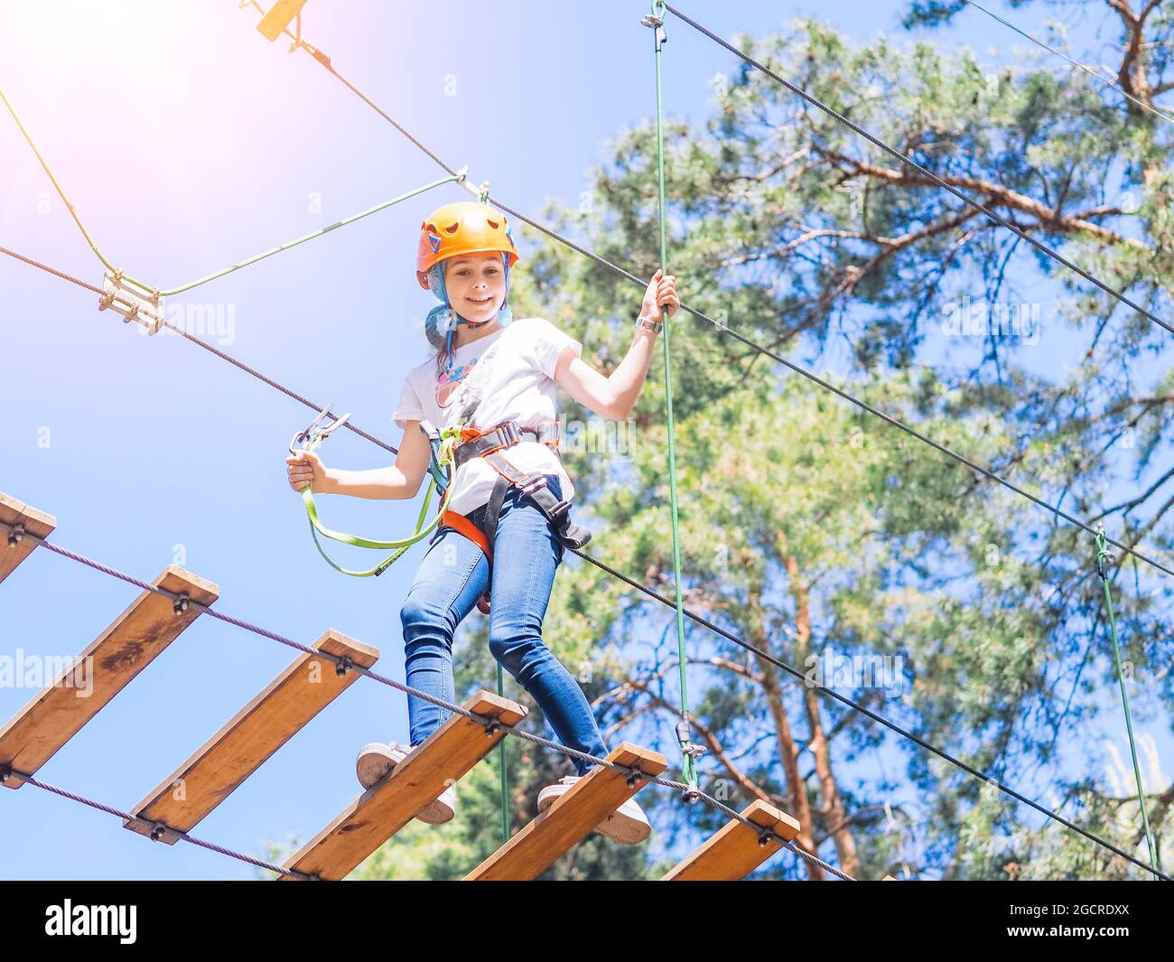 Kid in orange helmet climbing in trees on forest adventure park. Girl ...