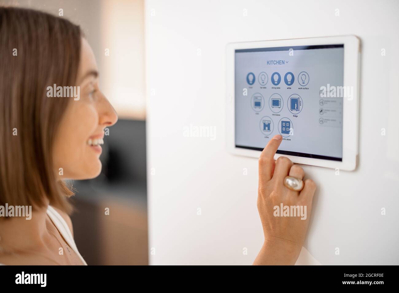Happy woman controlling smart devices using control panel at kitchen ...