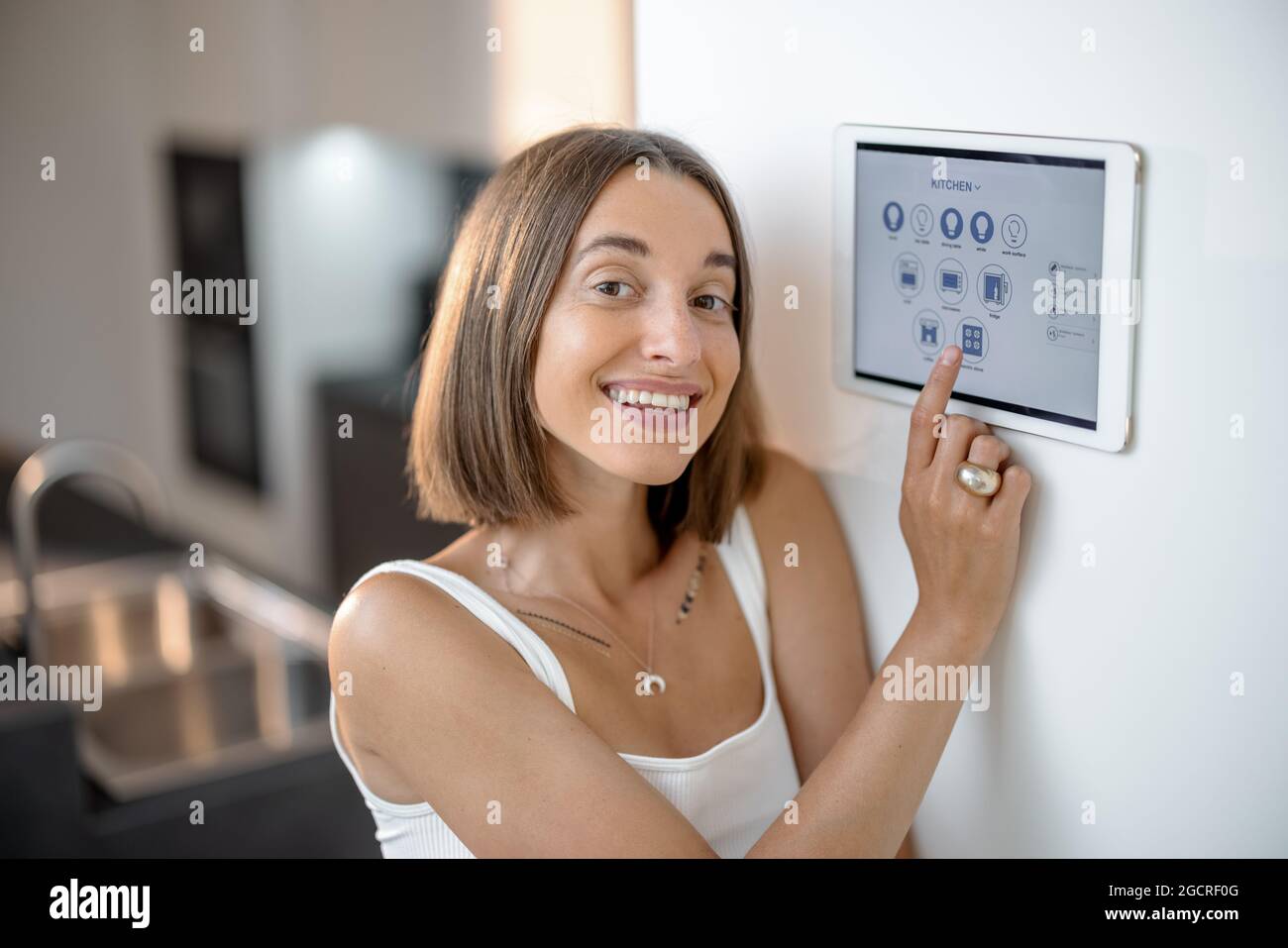 Happy woman controlling smart devices using control panel at kitchen ...