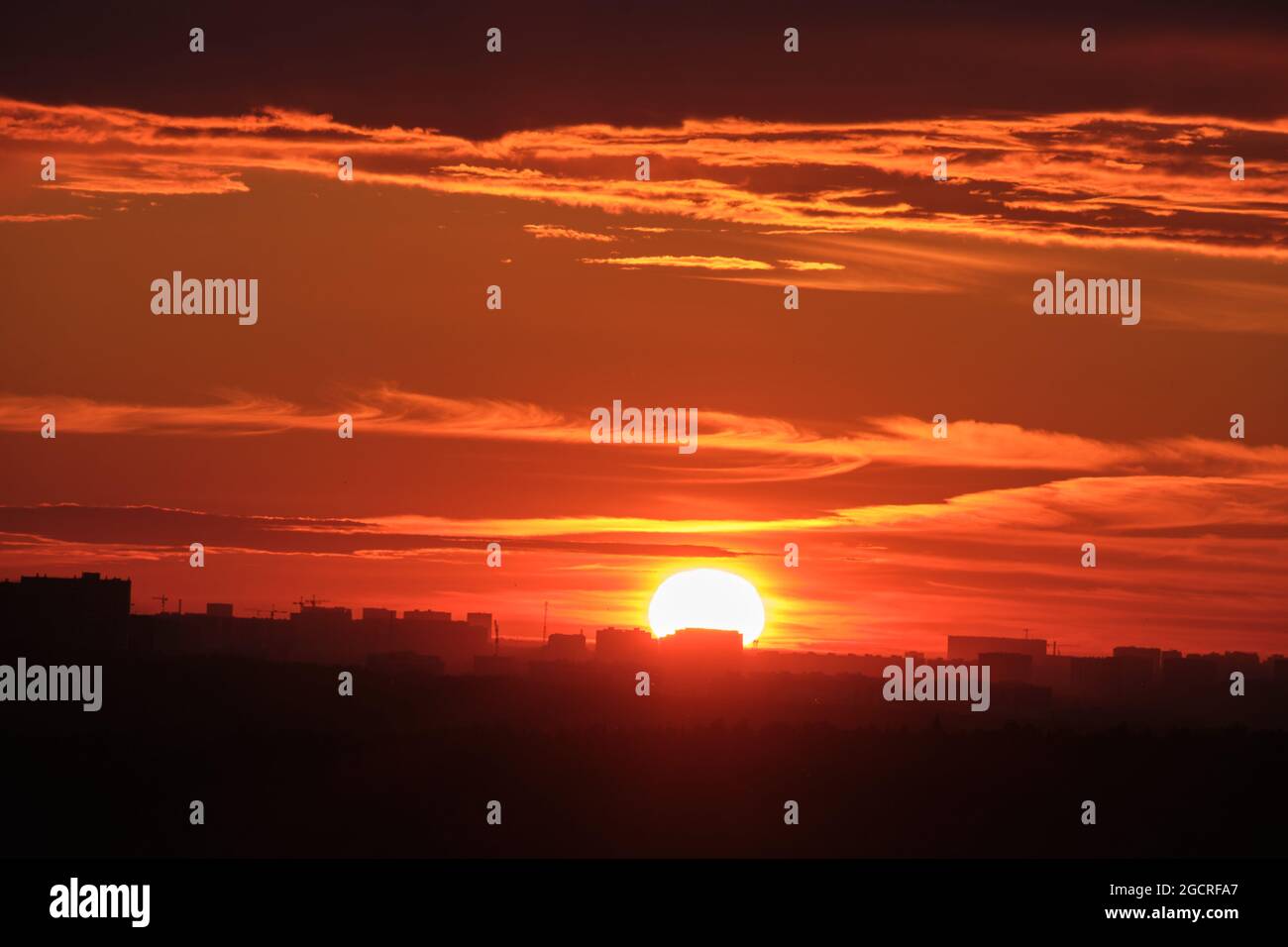 The big red sun sets at sunset behind the evening houses on the horizon ...