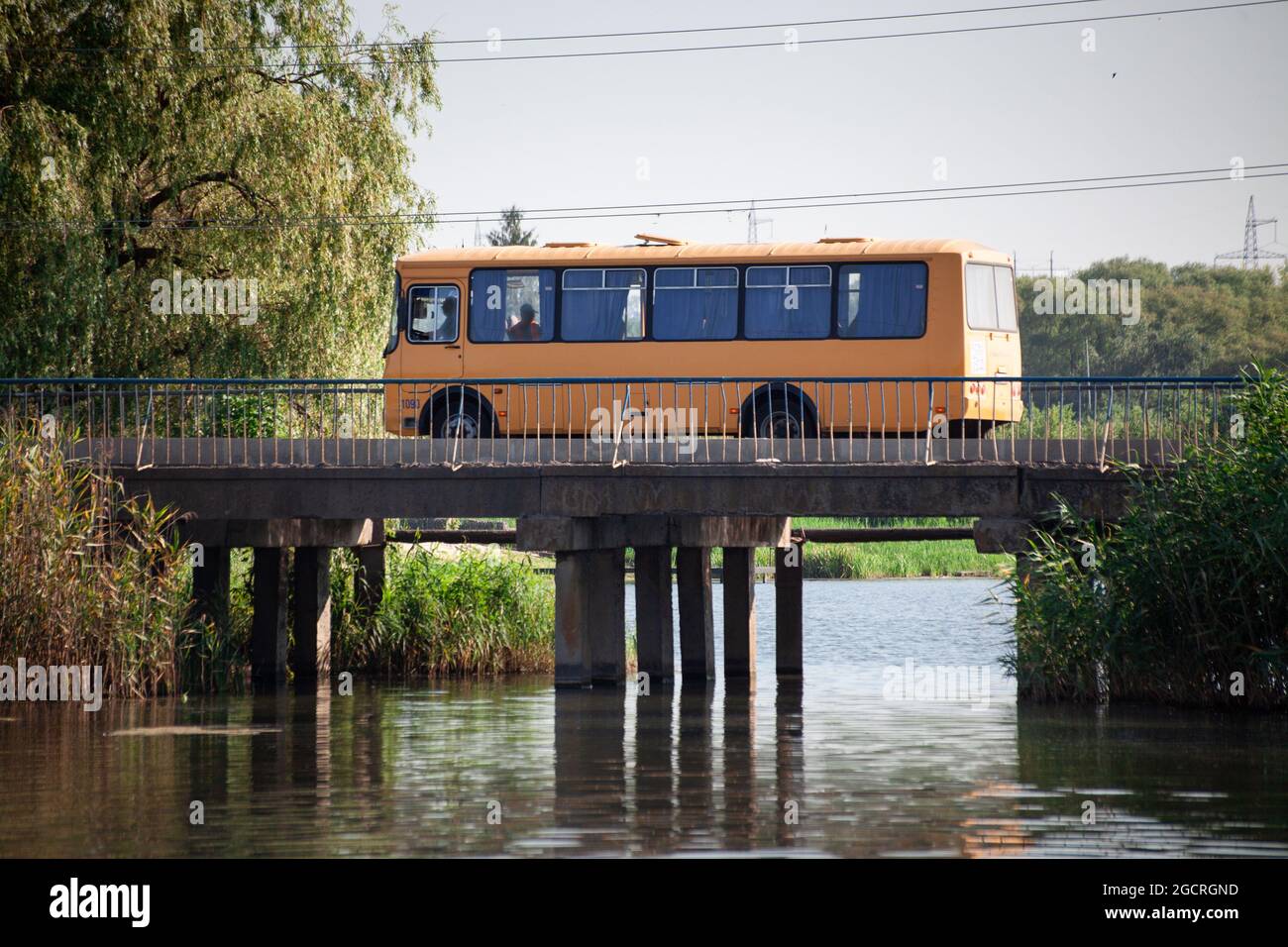 Orange bus on concrete bridge over a small river with green reeds. Road ...