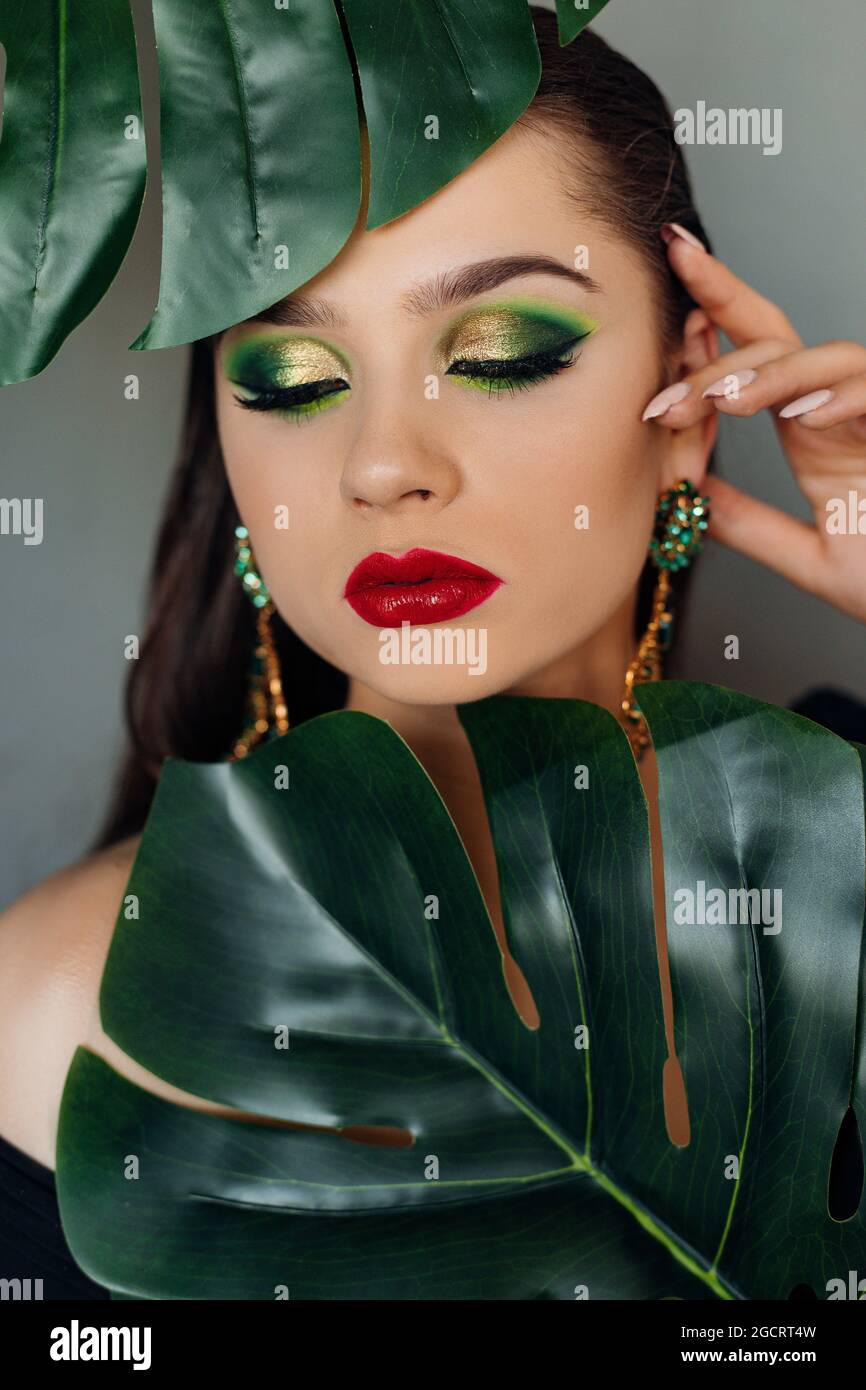 Close up face of beautiful young woman covering by green monstera green ...