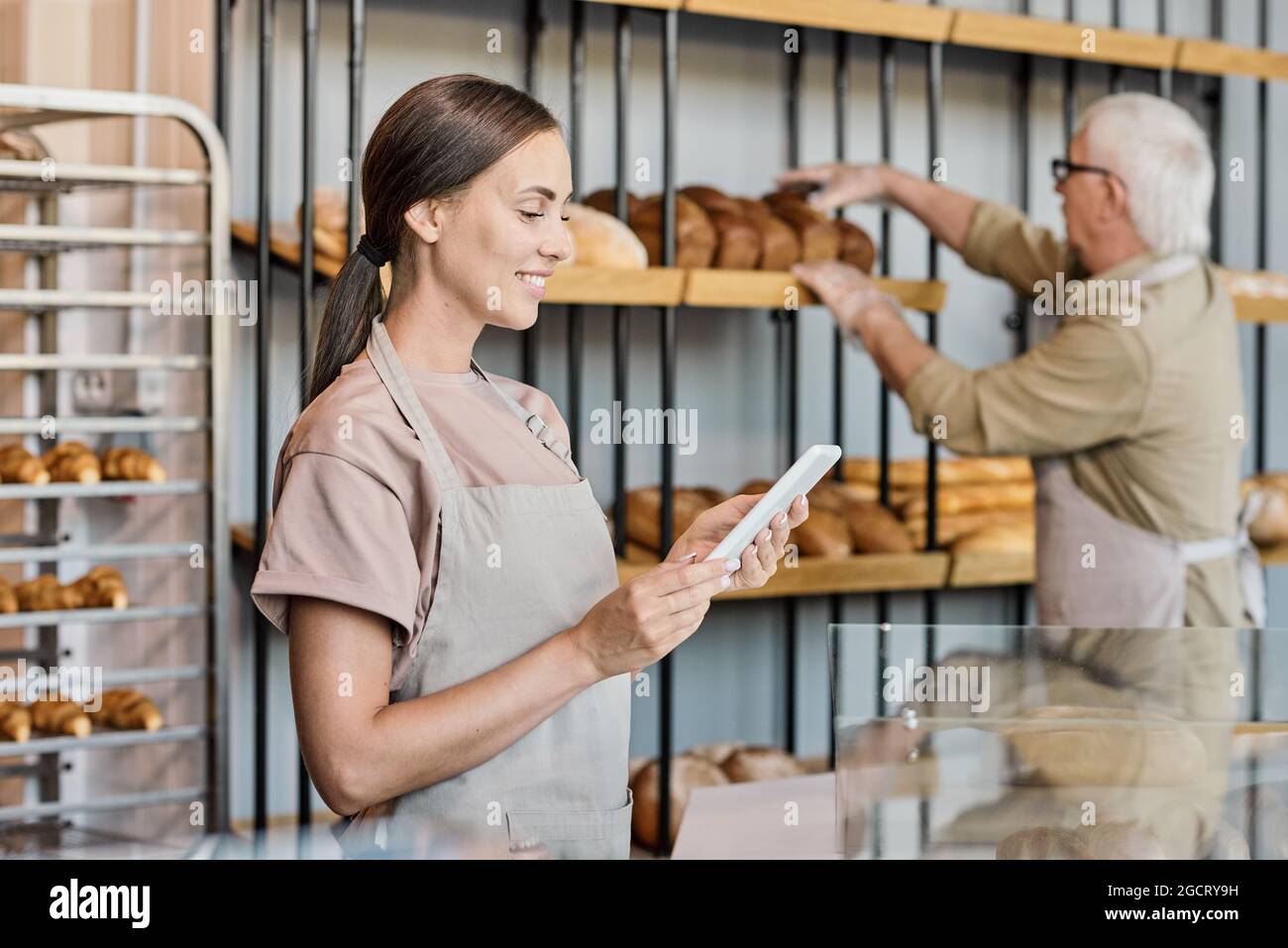 Happy female clerk looking through prices for bread against mature man ...