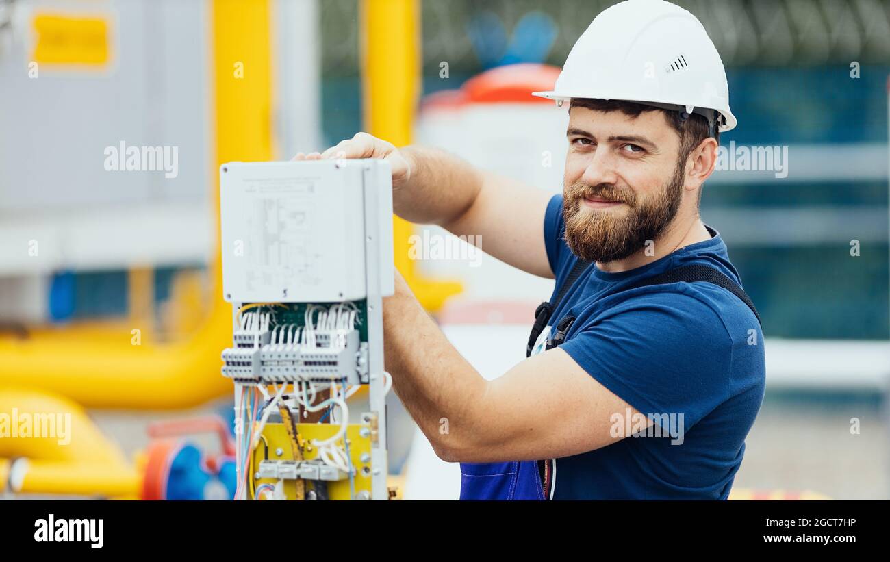 Electrician in a helmet and overalls works adjusts the equipment looks ...