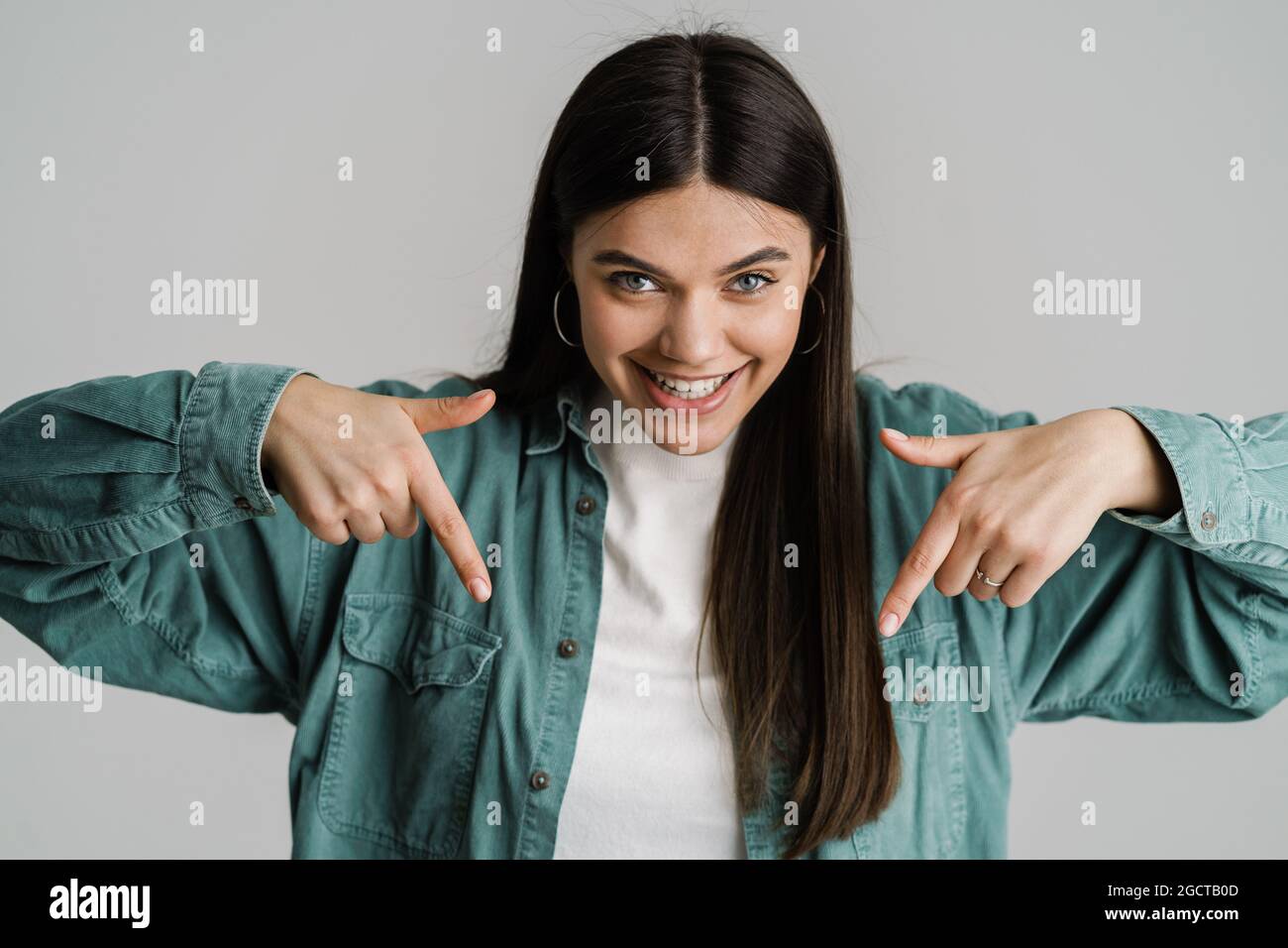 Young brunette woman smiling and pointing fingers downward isolated ...