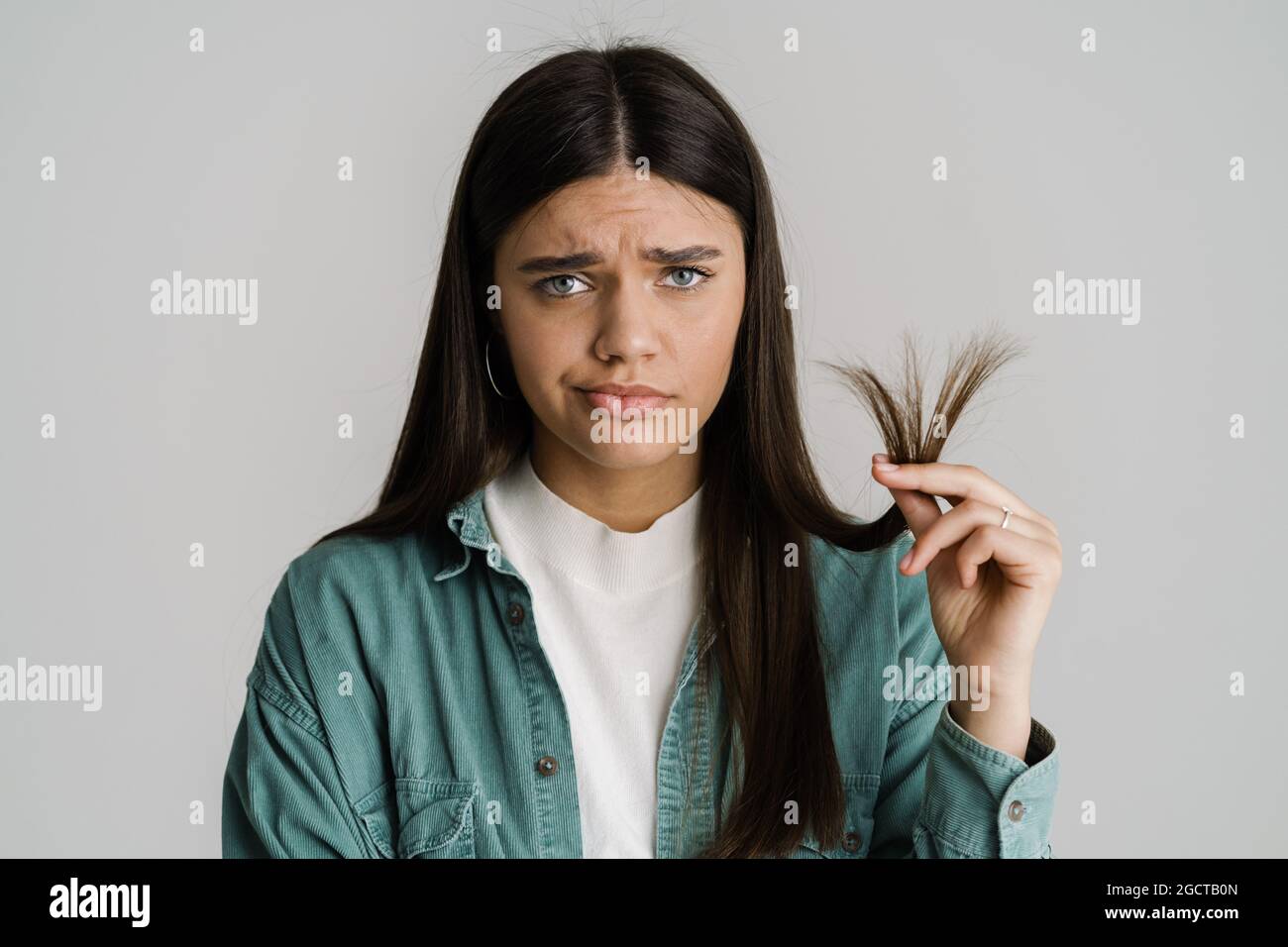 Young confused woman frowning and showing lock of her hair isolated ...