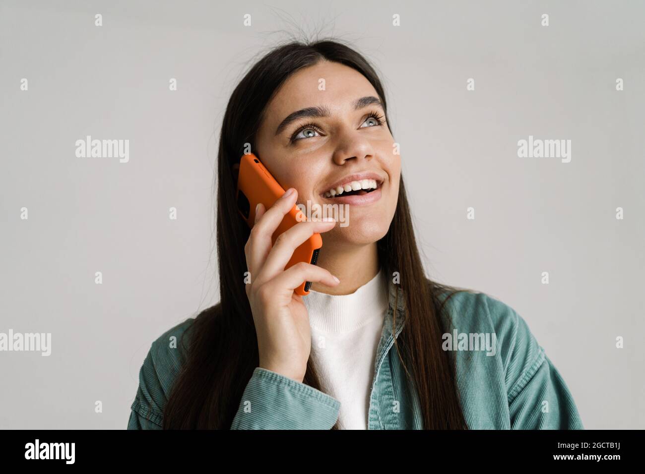 Young brunette woman smiling while talking on mobile phone isolated ...