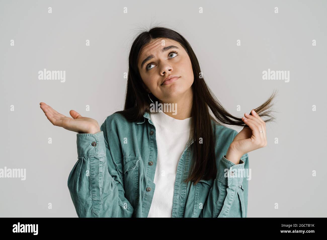 Young confused woman holding copyspace and lock of her hair isolated ...