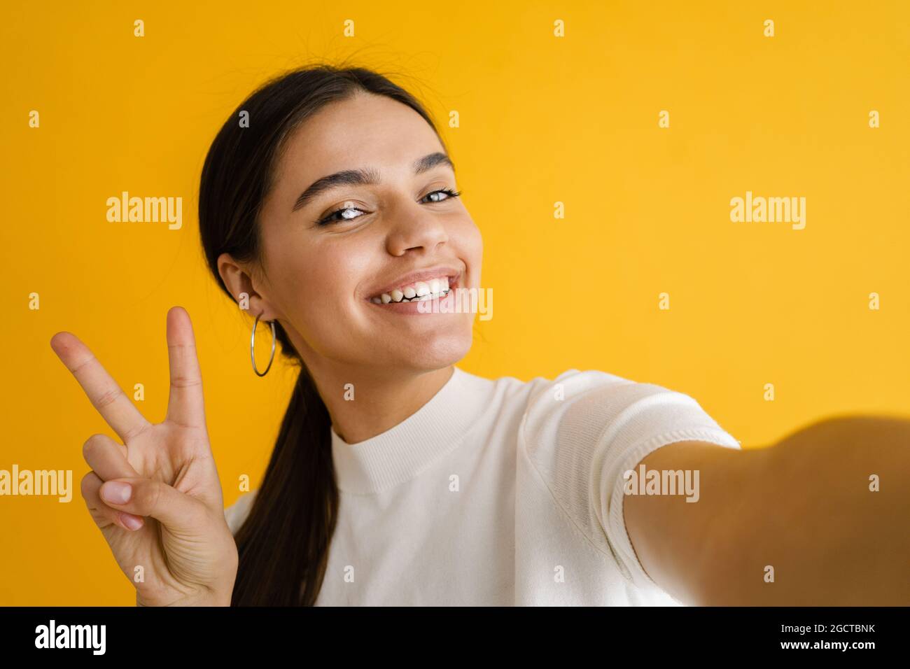 Young smiling woman showing peace sign while taking selfie photo ...