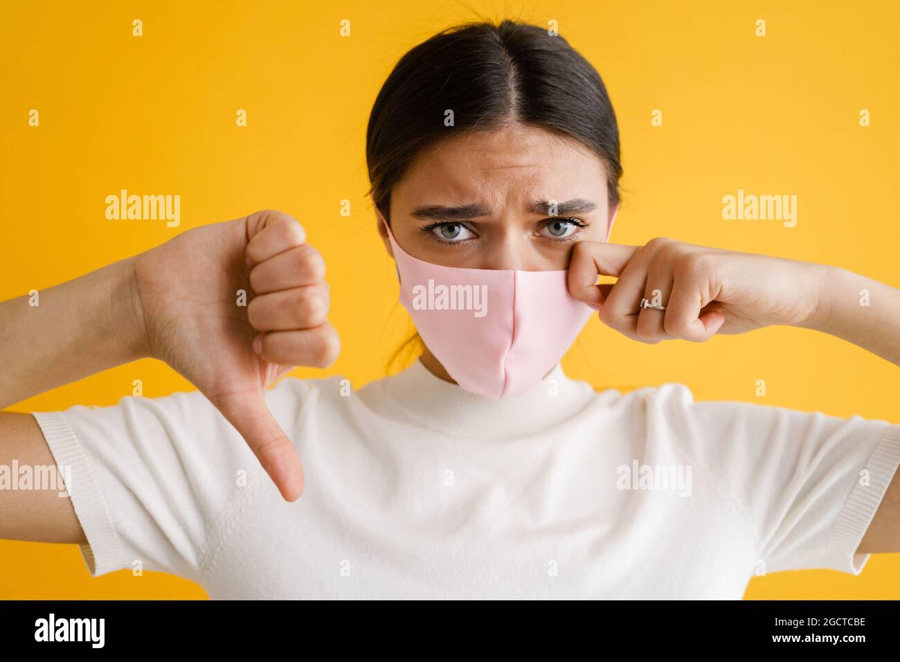 Young brunette woman in face mask crying and showing thumb down ...