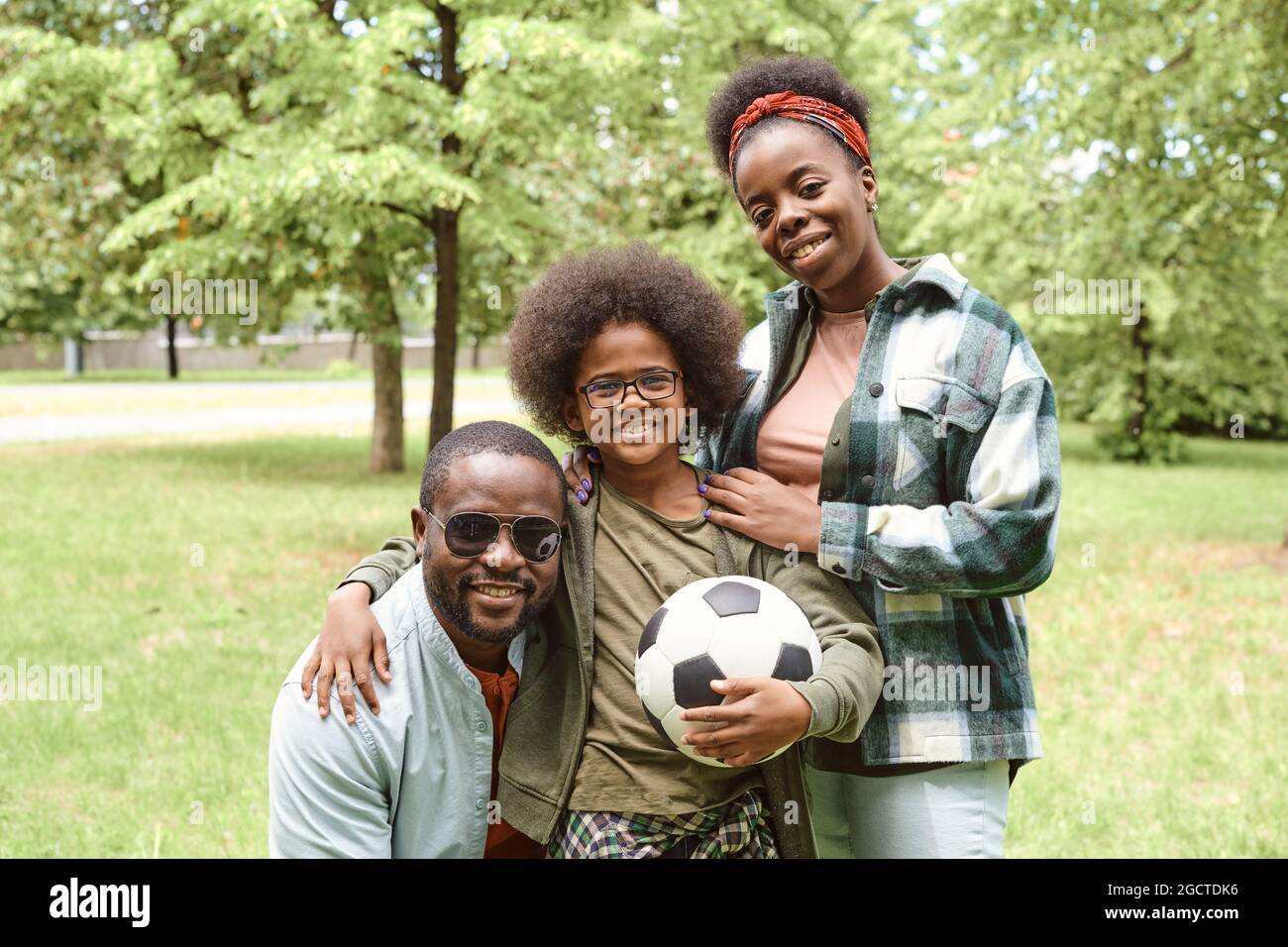 Happy little boy with ball and his parents standing in front of camera ...