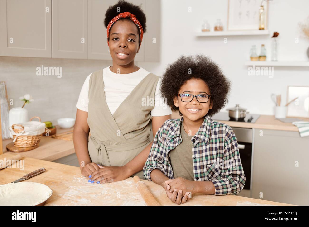 Happy mother and son standing by kitchen table while cooking pastry ...