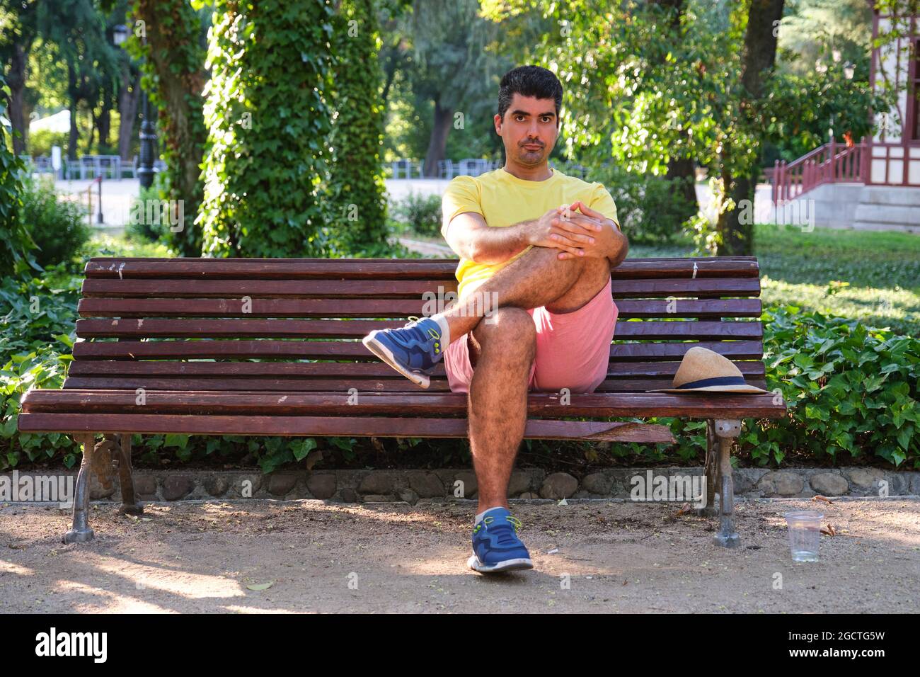 Man sitting on a bench with the legs crossed and looking at camera ...