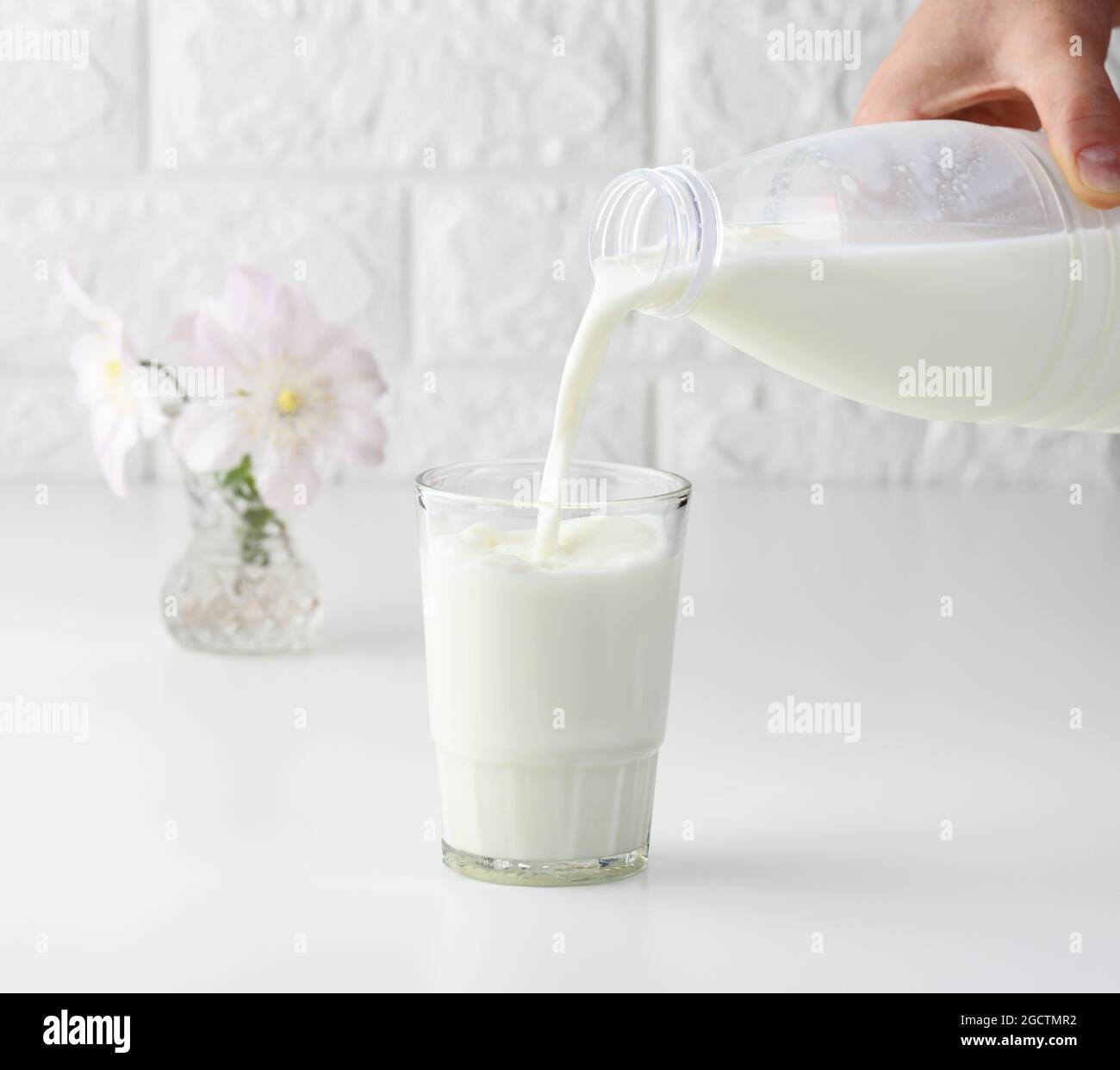 process of pouring fresh milk from a plastic bottle into a glass cup ...