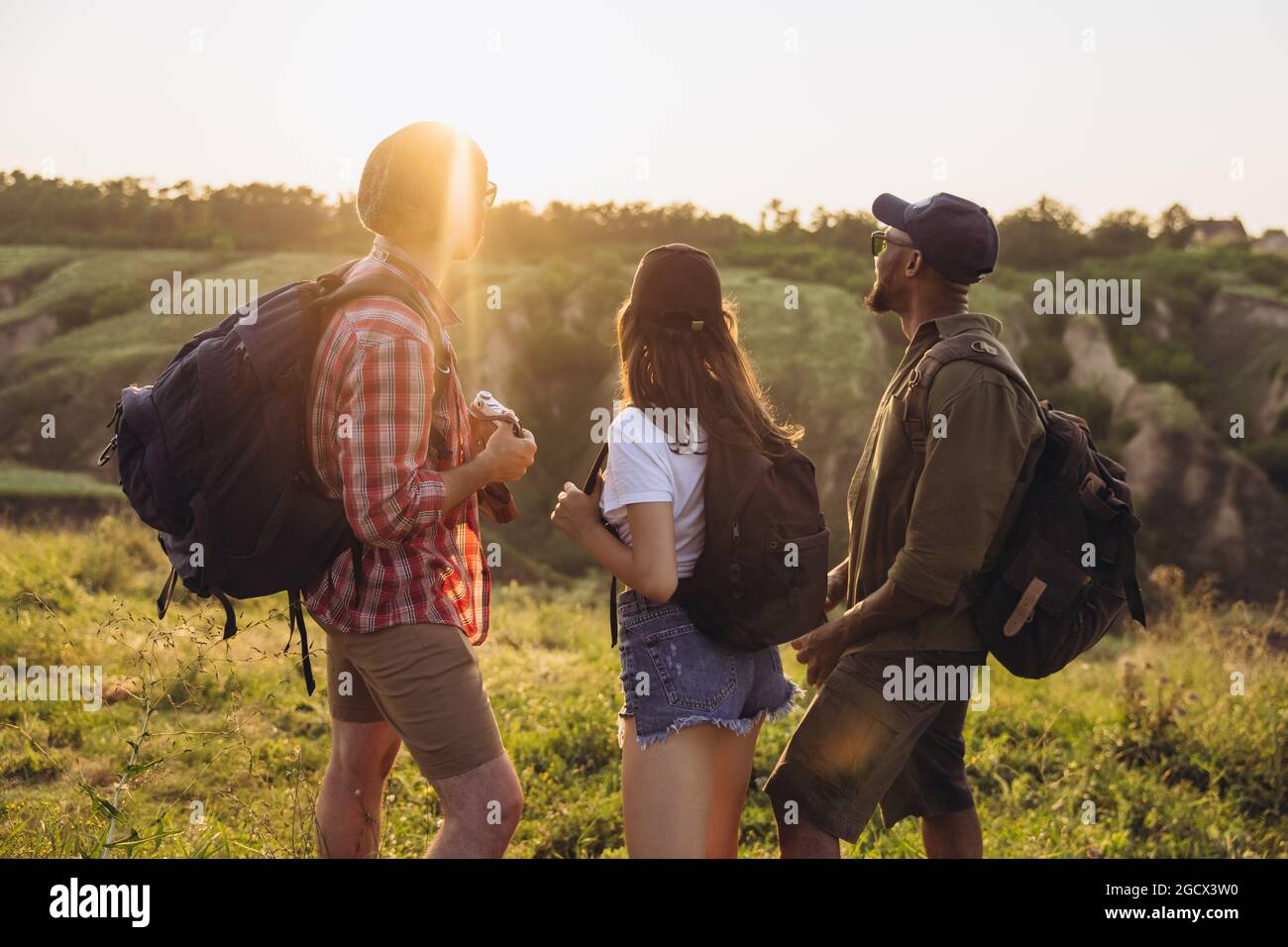 Group of friends, young men and woman walking, strolling together in summer forest, meadow ...