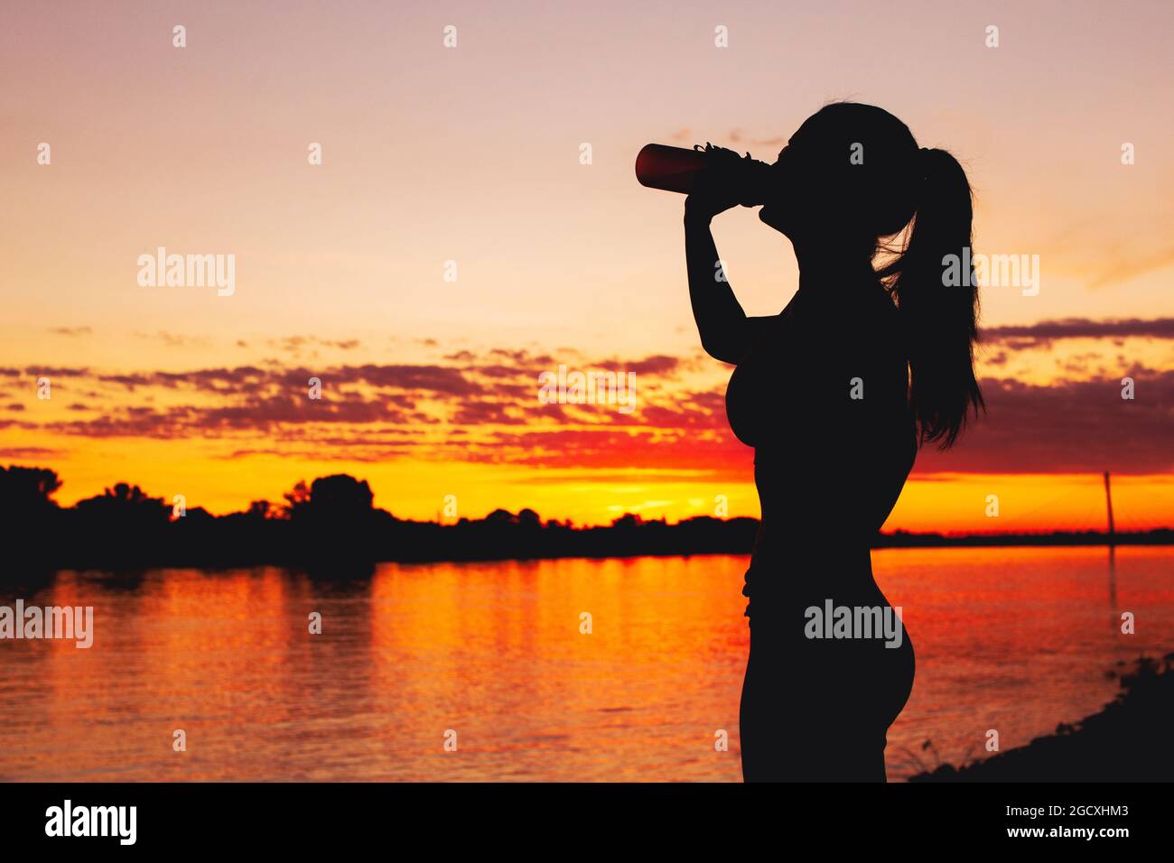 Thirsty young woman silhouette drinking refreshment from bottle at ...