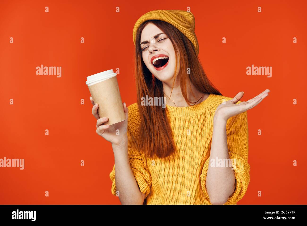 pretty woman in yellow hat with a cup of hot drink in hands emotions ...