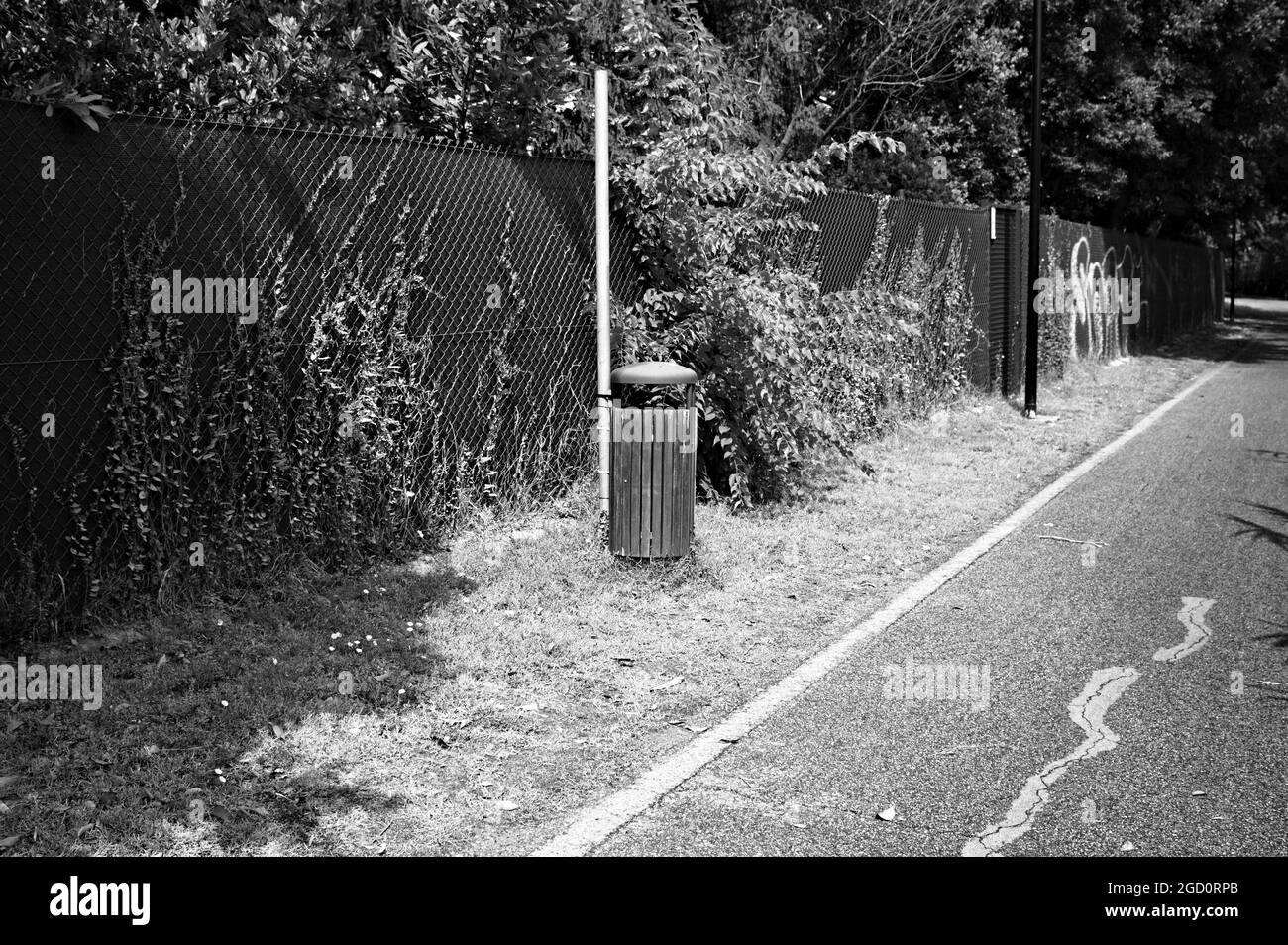 A wooden and metal garbage can on the edge of a pedestrian walkway in a ...