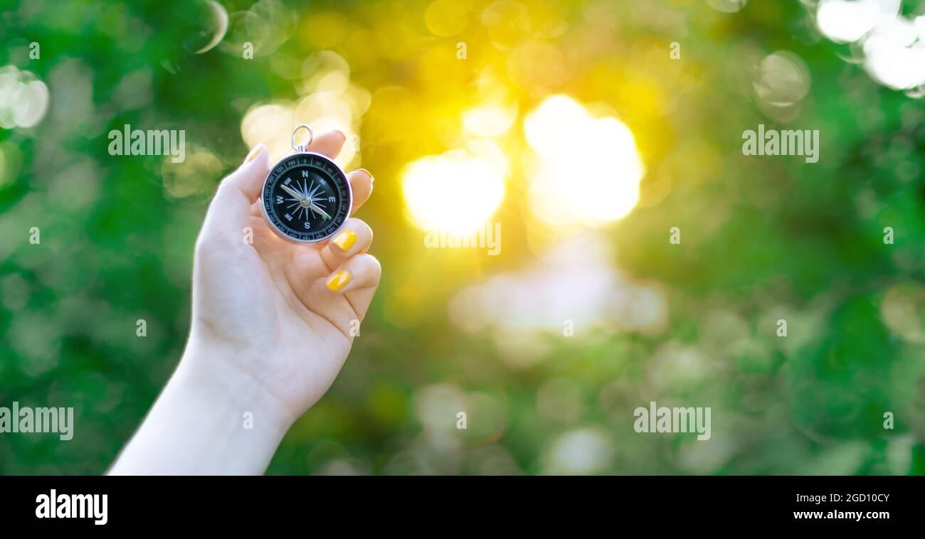 Hand with compass on green blurred background with sun glare at sunset ...
