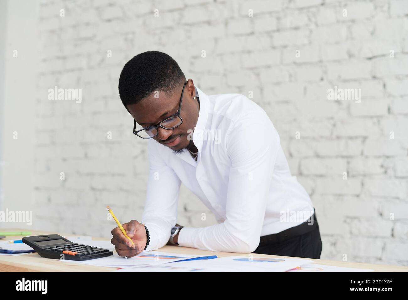 Young african executive in shirt stands at his desk in the office ...