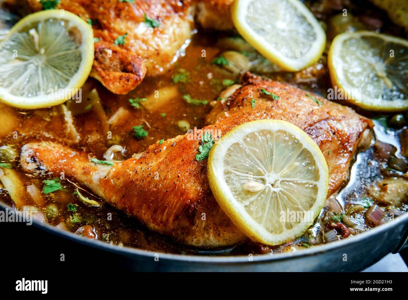 Cooking Italian split chicken leg piccata in large pan on kitchen stove ...