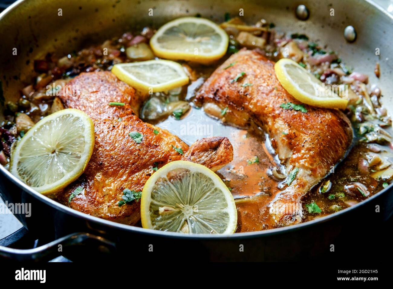 Cooking Italian split chicken leg piccata in large pan on kitchen stove ...