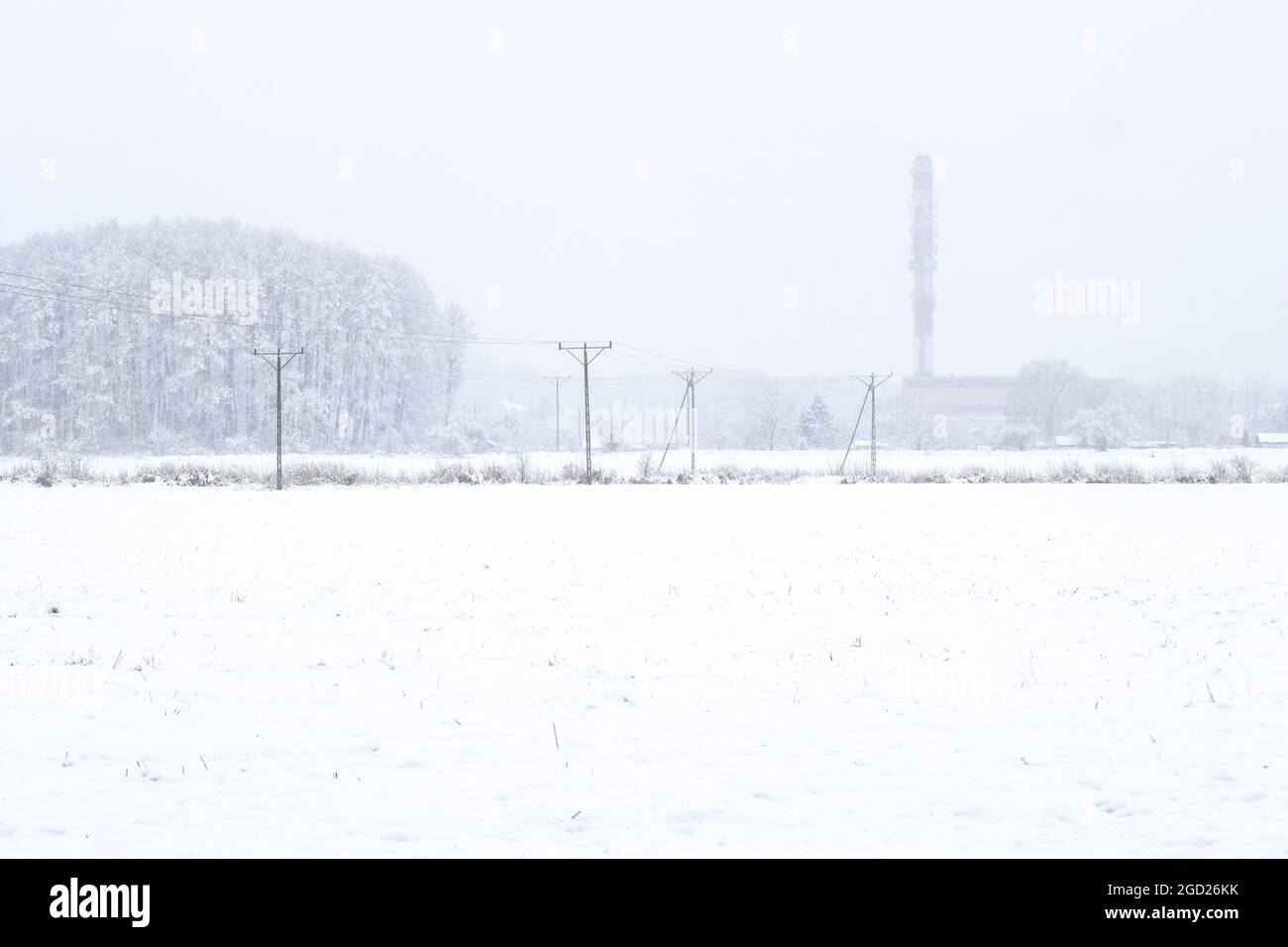 Field covered with snow in winter during snowfall with factory in ...