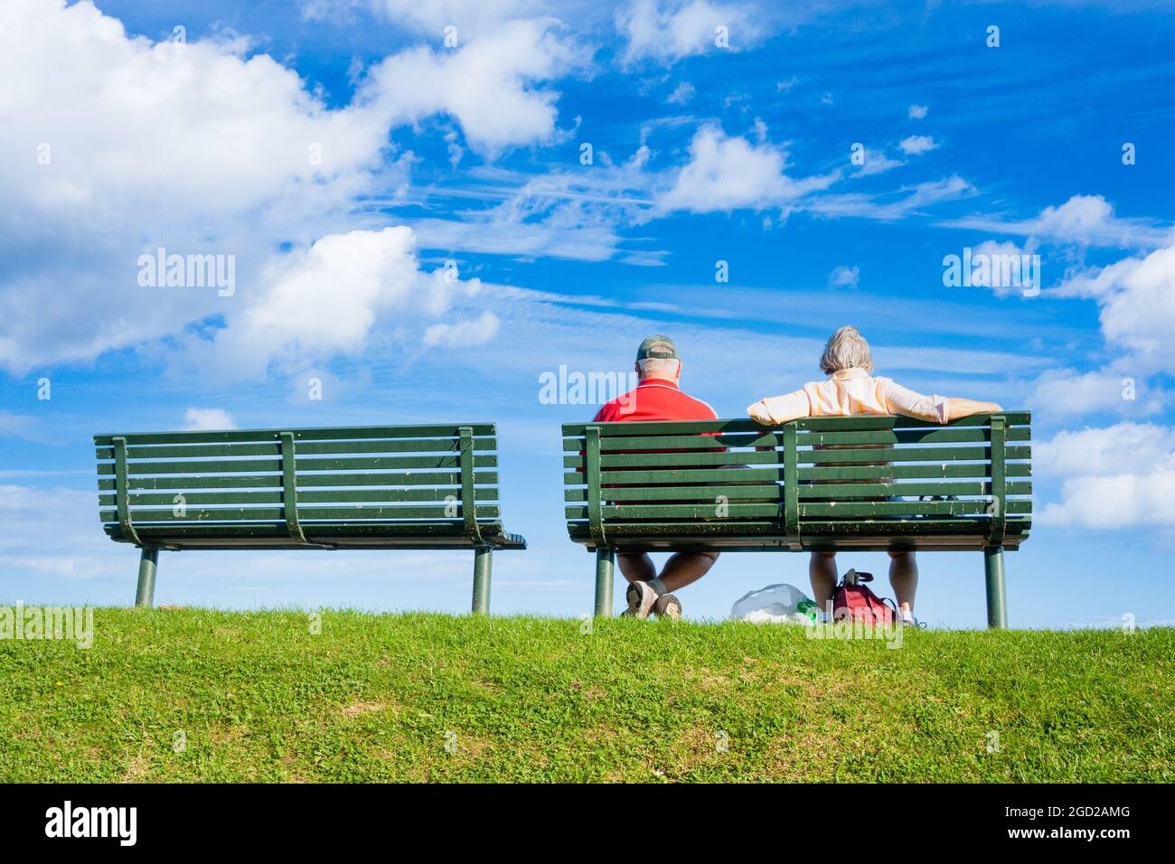 Rear view of elderly couple sitting on seat overlooking the sea on a ...
