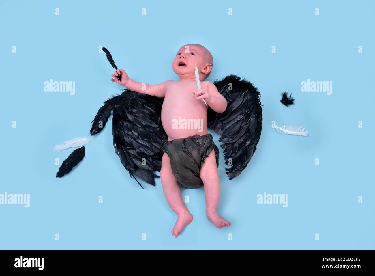 A newborn baby boy with black demon wings on a blue studio background ...